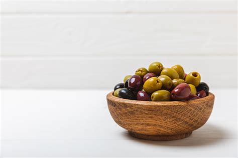 하얀 나무 배경에 녹색 검정색 빨간색 올리브 그릇에 담긴 다양한 종류의 올리브와 신선한 올리브 잎을 곁들인 올리브 오일 복사 공간 텍스트를 위한 위치입니다 지중해 음식 채식