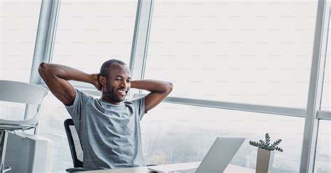 기쁨을 느낍니다 쾌활한 젊은 아프리카계 미국인 사업가가 의자에 기대어 손을 머리 뒤로 잡고 활짝 웃으며 화면을 보고 있다 사진 Unsplash의 테이블 이미지