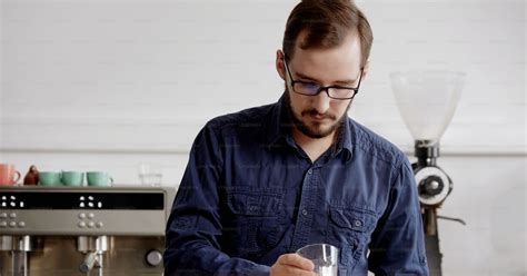 유리 컵에서 갓 내린 커피를 맛보고 숟가락을 사용하여 바로스타에 대한 커피 커핑 테스트에서 커피 맛과 풍미를 검사하는 남자의 손을 닫습니다 사진 Unsplash의