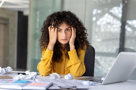 서류와 노트북으로 둘러싸인 책상에 앉아 스트레스를 받는 여성 사업가가 현대 사무실 환경에서 업무 관련 스트레스를 겪고 있습니다 걱정하는에 대한 스톡 사진 및 기타 이미지