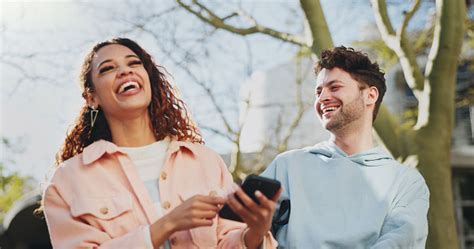 전화 재미 있고 야외에서 데이트 여행 및 도시에서 함께 밈을 웃는 커플 모바일 행복한 남자와 인종 간 여자 공원에서 농담을위한 온라인 앱 소셜 미디어에서 비디오 및 코미디
