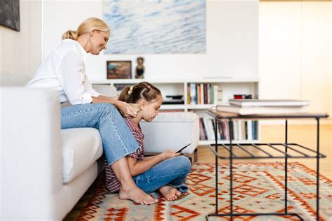 White Girl Using Tablet Computer While Her Mother Doing Hairstyle For