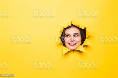 이빨이 나는 미소를 가진 기쁜 청년은 긍정적으로 옆으로 보이며 빈 공간이있는 노란색 배경 위에 고립 된 종이 구멍에 얼굴을 보여줍니다 긍정적 인 감정 찢어진 종이를 들여다