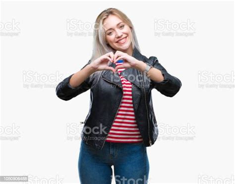 젊은 금발 여자 마음 기호와 손으로 모양을 보여주는 사랑에 웃 고 고립 된 배경 위에 검은 자 켓을 입고 낭만적인 개념입니다