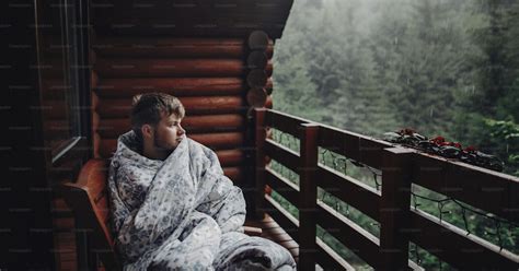 산속의 숲을 배경으로 비오는 날 나무 오두막의 현관에서 담요를 덮고 있는 세련된 남자 여행자 세련된 힙 스터 휴식 텍스트