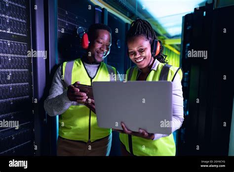 Happy African American Computer Technicians Wearing Headphones Using Laptop Working In Server