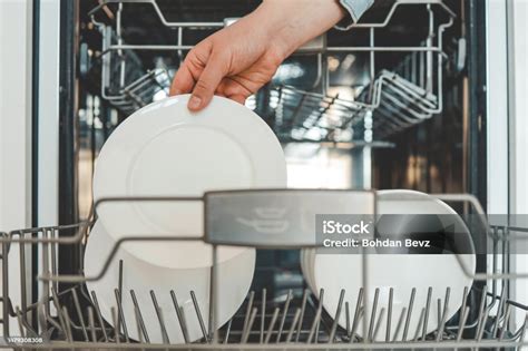 식기 세척기를 식기로 접시에 담거나 비우거나 내리는 여성 손 주방용품 라이프스타일 전망 여자는 접시를 식기 세척기에 넣거나 꺼냅니다 주부는 집안일을한다 가득 찬에 대한 스톡