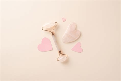 스킨 케어 미용 컨셉으로 셀프 케어 루틴을 향상시키고 고요한 파스텔 베이지색 배경에 작은 핑크색 하트가 있는 페이스 롤러와