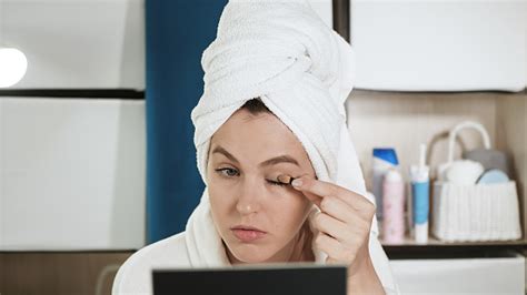 소녀는 얼굴에 아이 섀도우를 적용합니다 젊은 매력적인 여자 흰색 수건과 욕실목욕 가운은 눈꺼풀 오른쪽 눈에 그림자를 넣습니다 미용사 집에서만 컨셉으로 메이크업 클로즈업 25