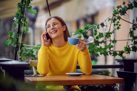 카페 테라스에 앉아 커피 한 잔을 들고 친구와 전화 통화를 하는 웃는 갈색 머리 노랑에 대한 스톡 사진 및 기타 이미지 노랑 레스토랑 사람들 Istock