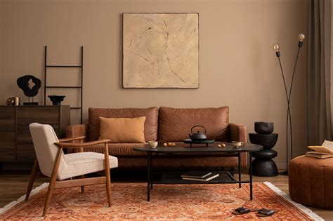 모형 포스터 프레임 갈색 소파 부클 안락의자 둥근 푸프 나무 찬장 슬리퍼 및 개인 액세서리가 있는 거실 인테리어의 세련된 구성