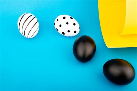 파란색 배경에 검은 색과 흰색 계란 배경에 노란색 밝은 악센트입니다 기하학적 패턴의 흰 달걀 부활절 휴일 부활절 기분 부활절을위한 예술 사진입니다 부활절 배경입니다 0명에