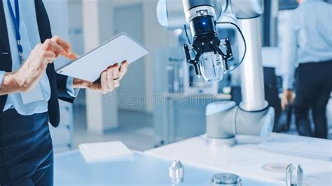 Stylish Female Industrial Robotics Engineer Uses Tablet Computer To Program And Manipulate Robot