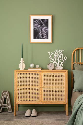 현대적인 침실 인테리어의 세련된 구성 포스터 프레임 등나무 Commode 아름다운 침구 및 창조적 인 개인 액세서리를 모의하십시오 녹색 벽 템플렛 공간을 복사합니다 침실에