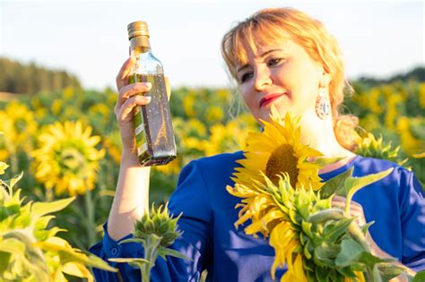 갈색 머리를 한 소녀가 손에 식물성 기름 한 병을 들고 있다 파란 드레스를 입은 한 여성이 해바라기 꽃 들 사이에 서 있다 가을에 대한 스톡 사진 및 기타 이미지 Istock