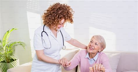 노인 여성이 거실의 소파에서 일어나도록 돕는 여성 간병인 웃는 간호사가 노인 여성이 일어나도록 돕고 있다 소파에서 일어나는 동안 환자를 지원하는 돌보는 간호사 사진