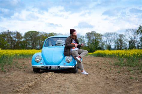 검은 재킷과 회색 바지를 입은 남자가 파란색 폭스바겐 비틀에 앉아 사진 Unsplash의 무료 가수 이미지