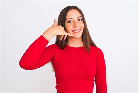 고립 된 흰색 배경 위에 서있는 빨간 캐주얼 티셔츠를 입은 어린 아름다운 소녀는 전화통화처럼 손과 손가락으로 전화 제스처를하고 미소 짓고 있습니다 개념을 전달합니다 T