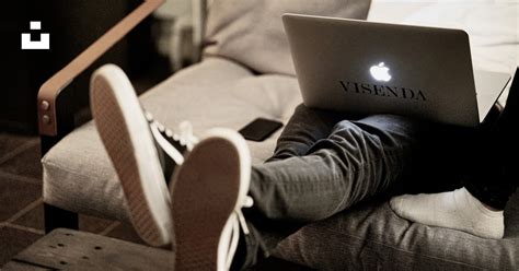 흰색 긴팔 셔츠와 파란색 데님 청바지를 입은 남자가 Macbook을 사용하여 갈색 소파에 앉아 있다 사진 Unsplash의 무료 사무실 이미지