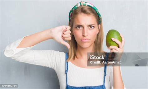 그런 지 위에 아름 다운 젊은 여자와 성 난 얼굴 아래로 엄지 싫어 보여주는 음수 부호 거부 개념 신선한 망고를 들고 벽 그레이 개념에 대한 스톡 사진 및 기타 이미지