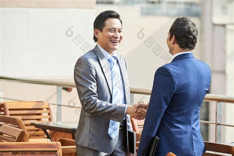 倚在栏杆上握手的两位商业人士图片 包图网