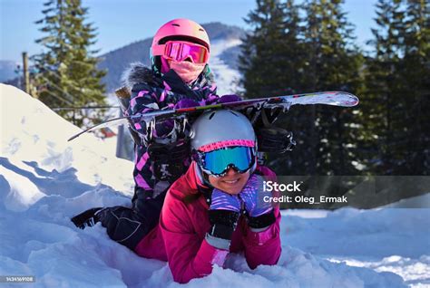 겨울을 즐기는 눈 속에 함께 누워있는 스키 장비의 어머니와 딸은 스키 리조트에서 즐거운 시간을 보내고 있습니다 스노우 보드로 눈 속에서 노는 행복한 가족 스키 여행에 대한