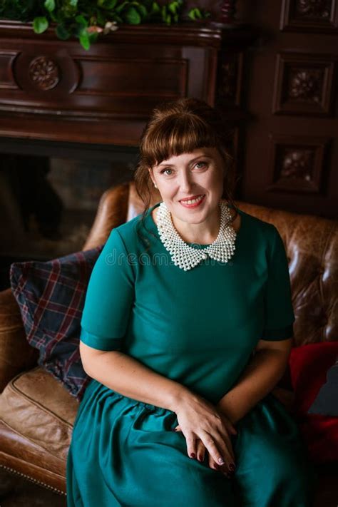 Friendly Mature Woman In Elegant Green Dress Sitting On Leather Sofa