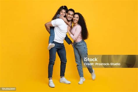 노란 배경을 통해 포즈를 취하는 쾌활한 중동 부모와 어린 딸의 초상화 가족에 대한 스톡 사진 및 기타 이미지 가족 전신 스튜디오 촬영 Istock