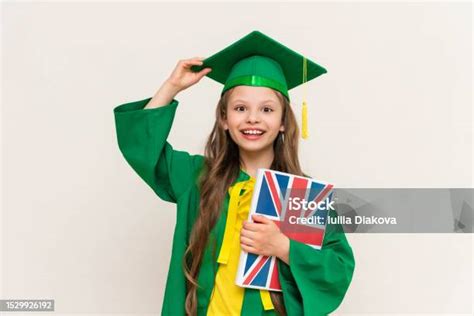 석사 복을 입은 학생이 영어로 영국 국기가 적힌 책을 들고 행복하게 웃고 있습니다 어린이를 위한 언어 교육 학교 영어 학교 졸업 흰색 격리 된 배경 영국 국기에 대한 스톡
