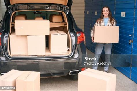 창고에 있는 차 트렁크 근처에 골판지 상자를 들고 웃는 아가씨 25 29세에 대한 스톡 사진 및 기타 이미지 25 29세 30 34세 Brand Name