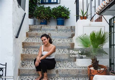검은 바지와 흰 티셔츠를 입은 젊은 여성이 하얗게 칠해진 흰 벽 가로 사진 공간을 복사하는 계단에 앉아있는 카메라를 본다 16 17 살에 대한 스톡 사진 및 기타 이미지