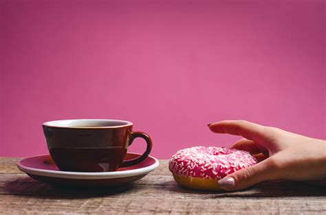 손을 들고 나무 테이블에 분홍색 배경에 뿌리와 다채로운 도넛 커피 한잔입니다 도넛의 두 종류입니다 케이크와 달콤한 음식 세부입니다 닫습니다 파스텔 컬러 건강관리와 의술에