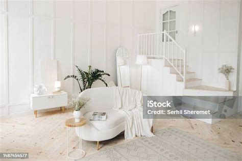 흰색 가죽 소파 플로어 램프 전체 길이의 타원형 거울 2층으로 이어지는 나무 계단이 있는 세련된 흰색 거실 아파트의 계단 집에서
