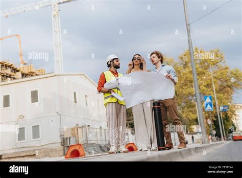 Adult Architects And Engineers Discussing A New Project Outdoors They Review Blueprints