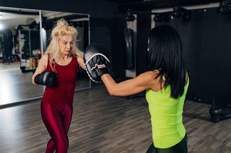 중년 여성은 체육관에서 개인 트레이너와 함께 훈련하고 권투 글러브를 착용하고 펀치를 날립니다 2명에 대한 스톡 사진 및 기타 이미지 Istock