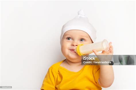 노란색 티셔츠와 흰색 배경에 모자를 입은 귀여운 행복한 백인 아기 소년의 초상화 아이는 카피 스페이스와 병에서 우유를 마십니다