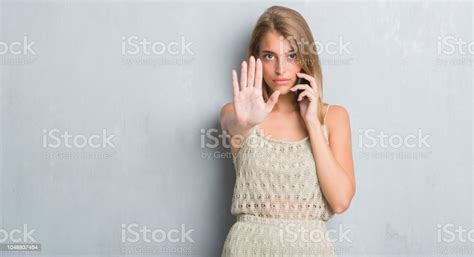 그런 지 회색 벽에 말하기와 전화를 통해 아름 다운 젊은 여 자가 심각 하 고 자신감 표현 방어 제스처 정지 표시를 하 고 손을 열합니다 경계 표지에 대한 스톡 사진 및