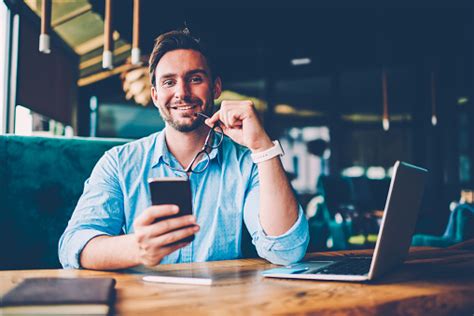 카페테리아 인테리어의 노트북 컴퓨터에서 원격으로 작업하는 4g에 연결된 현대 전화로 인터넷 응용 프로그램을 통해 결제하는 수염 성공적인 기업가의 절반 길이 초상화 극도의