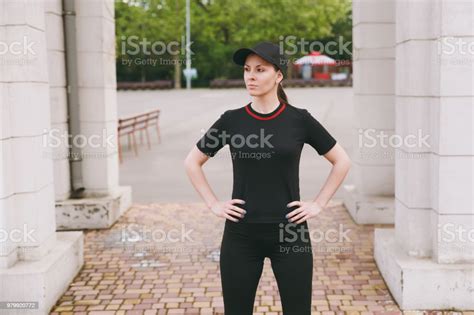영 운동 아름 다운 여 자가 검은 유니폼과 모자 스포츠 연습을 하 고 도시 공원 야외에 서 실행 하기 전에 워밍업에 집중 휘트니스 건강 한 라이프 스타일 개념입니다 가냘픈에
