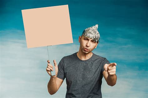 호일 모자를 쓴 괴짜 남자가 무서워서 손으로 손을 잡는다 넓은 눈과 입을 열고 파란색 배경에 스트라이크 포스터를 들고 있습니다 Popsicle Stick에 대한 스톡 사진