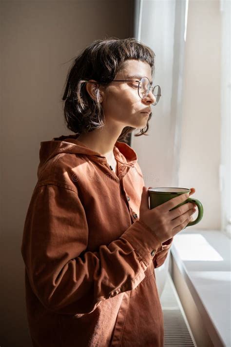 Teen Girl Nerd In Glasses Looking At Window Drinking Cup Of Tea At Home