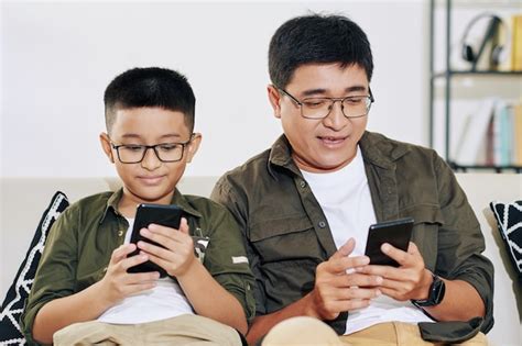 Premium Photo Preteen Son And His Mature Father Sitting On Sofa And Home And Playing Games On