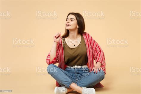 캐주얼 옷에 아름 다운 매력적인 젊은 여자의 초상화 스튜디오에서 파스텔 베이 지 벽 배경에 고립 된 옆을 보고 앉아 사람들은 진심으로 감정 라이프 스타일 개념입니다 복사