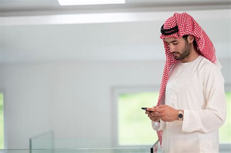 젊은 현대 무슬림 아라비아 사업가들은 집에서 스마트 폰을 사용하는 동안 전통적인 옷을 입고있다 고품질 사진 20 24세에 대한