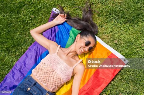 풀밭에 무지개 Lgbt 깃발을 들고 누워 있는 백인 갈색 머리 여자가 오른쪽을 바라보며 웃고 있다 Gay Pride Parade