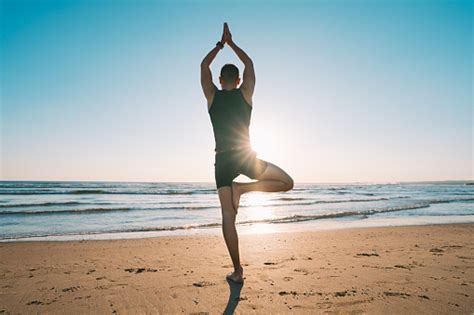 일몰 이나 일출에서 바다 전망해변에서 요가연습 남자 머리 위로 손을 들고 나무 포즈나 브르크사사나 휴식 자연과의 조화 건강한