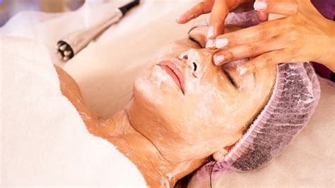 미용사는 여성 얼굴에 보습 마스크를 적용합니다 얼굴 관리를위한 미용 절차에 스파 살롱에있는 여성 미용 치료 치료를받는 백인 여성