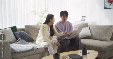 모던한 거실에서 소파에 앉아 노트북으로 온라인 쇼핑을 하는 젊은 커플 Stock ビデオ Adobe Stock