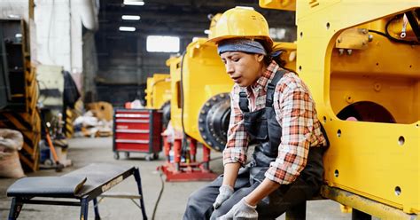 작업복과 안전모를 쓴 창고의 젊은 여성 노동자가 산업 기계 옆에 앉아 있는 동안 아픈 무릎을 만지고 있다 사진 Unsplash의 산업 이미지