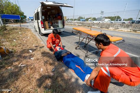 주황색 유니폼을 입은 두 명의 구급대원 또는 응급 의료 기술자가 들것 긴 척추 보드에 누워 있는 목과 머리 사고 피해자를 돕고 있습니다 교통사고 시 긴급 지원 1위에 대한